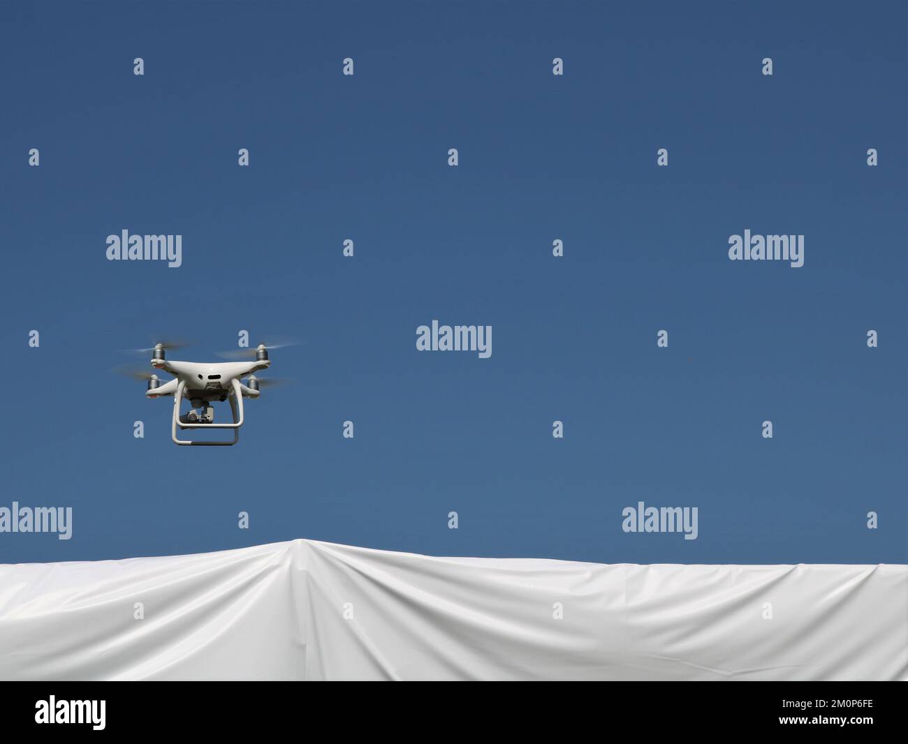 white drone in clear blue sky flying over white tent, launching copter ...