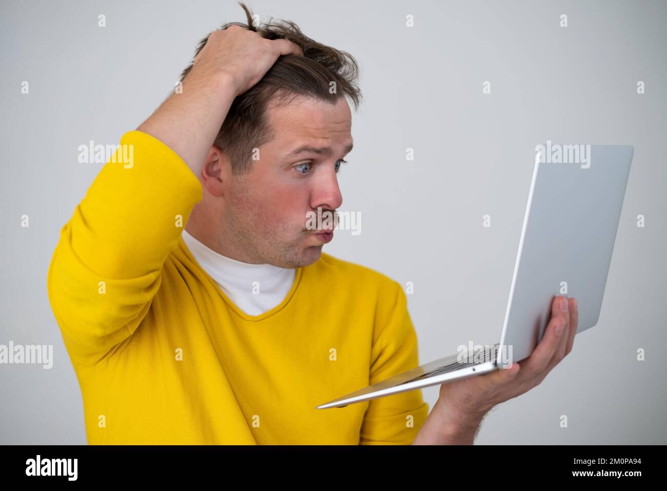Thinking young man standing with laptop looking on screen with confused ...