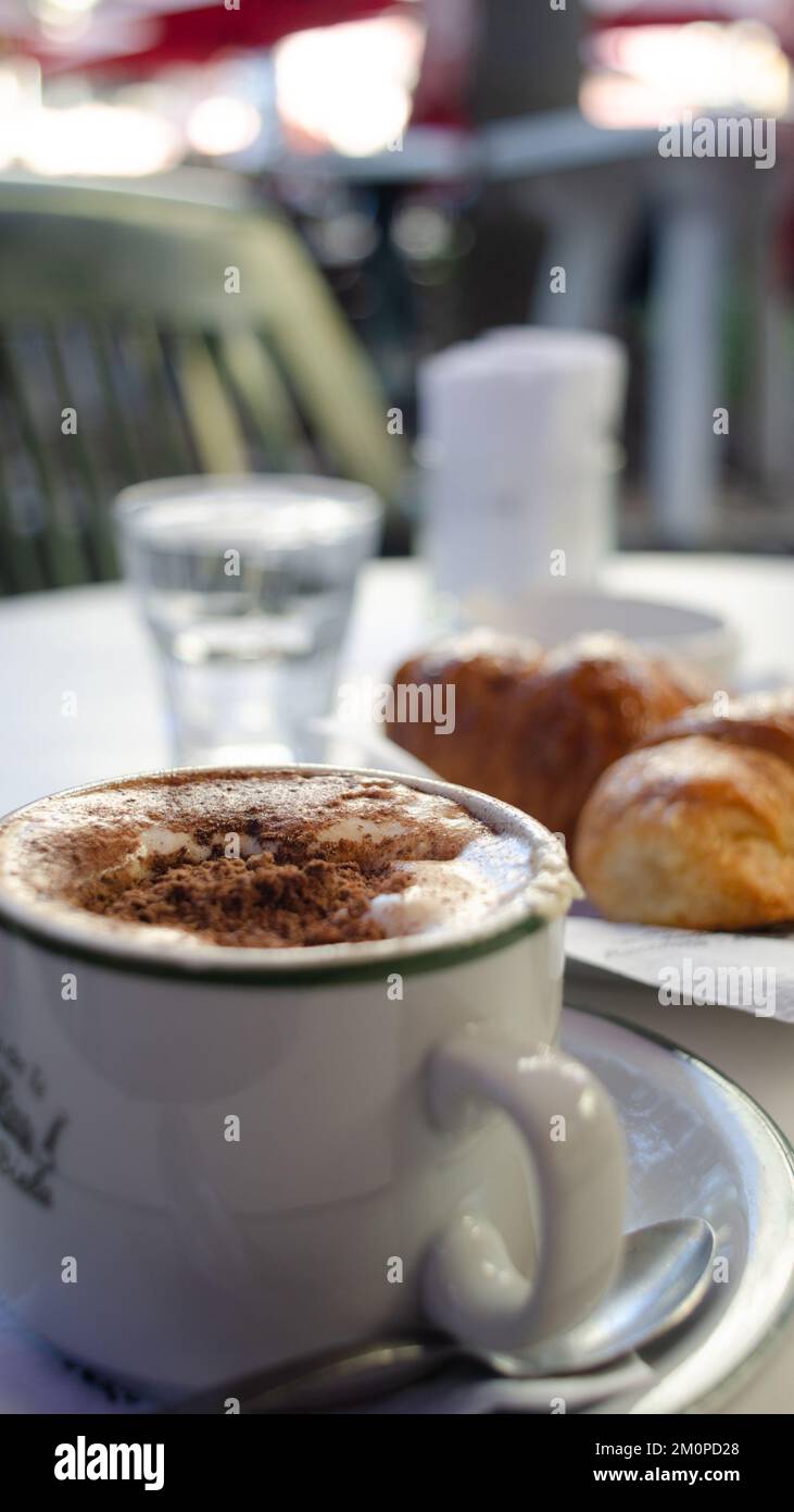 A vertical close-up shot of a cup of cappuccino and croissants on the ...