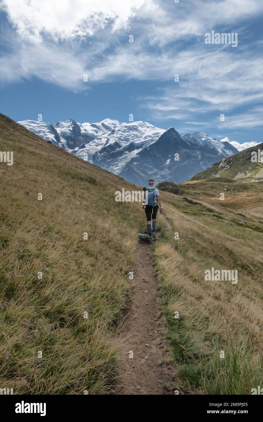 Single female walker moving along an alpine mountain trail in summer in ...