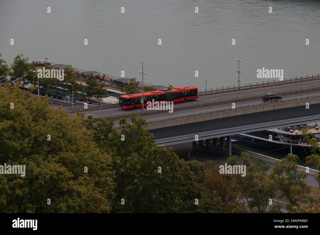 A high angle shot of a red bus and a car driving on a road over water ...