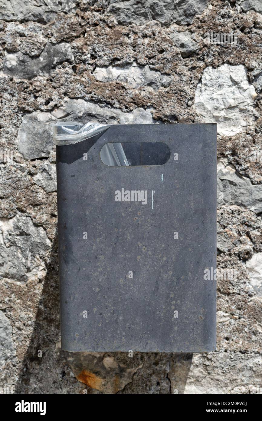 Vertical photo of grey metal trash can on stone wall in background ...