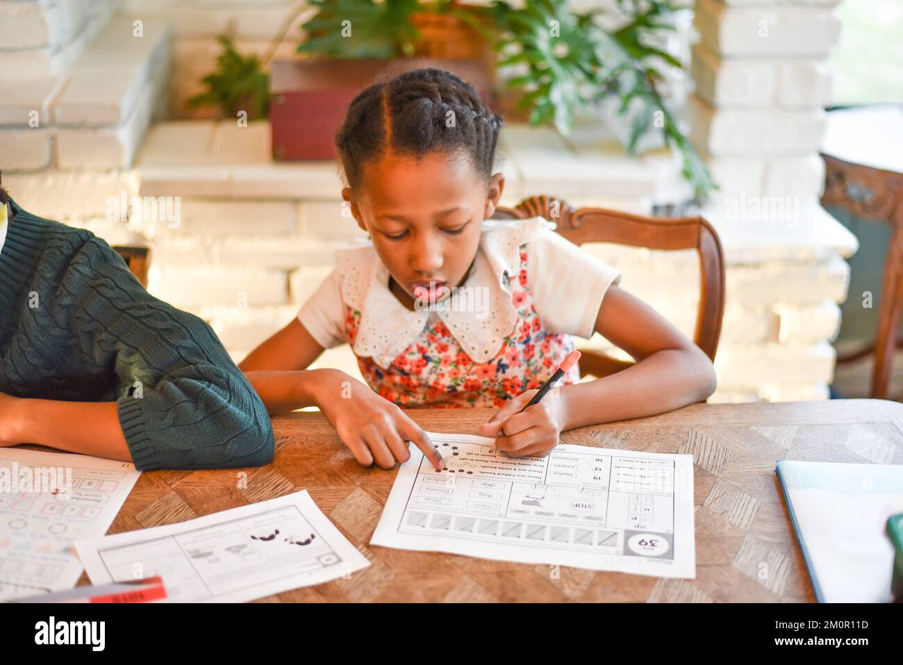 little girl doing homework at home while sitting at the kitchen table ...