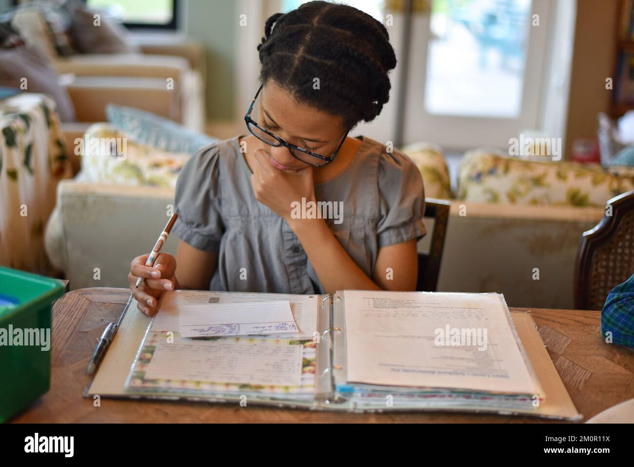 Teen girl doing homework at home while sitting at the kitchen table ...