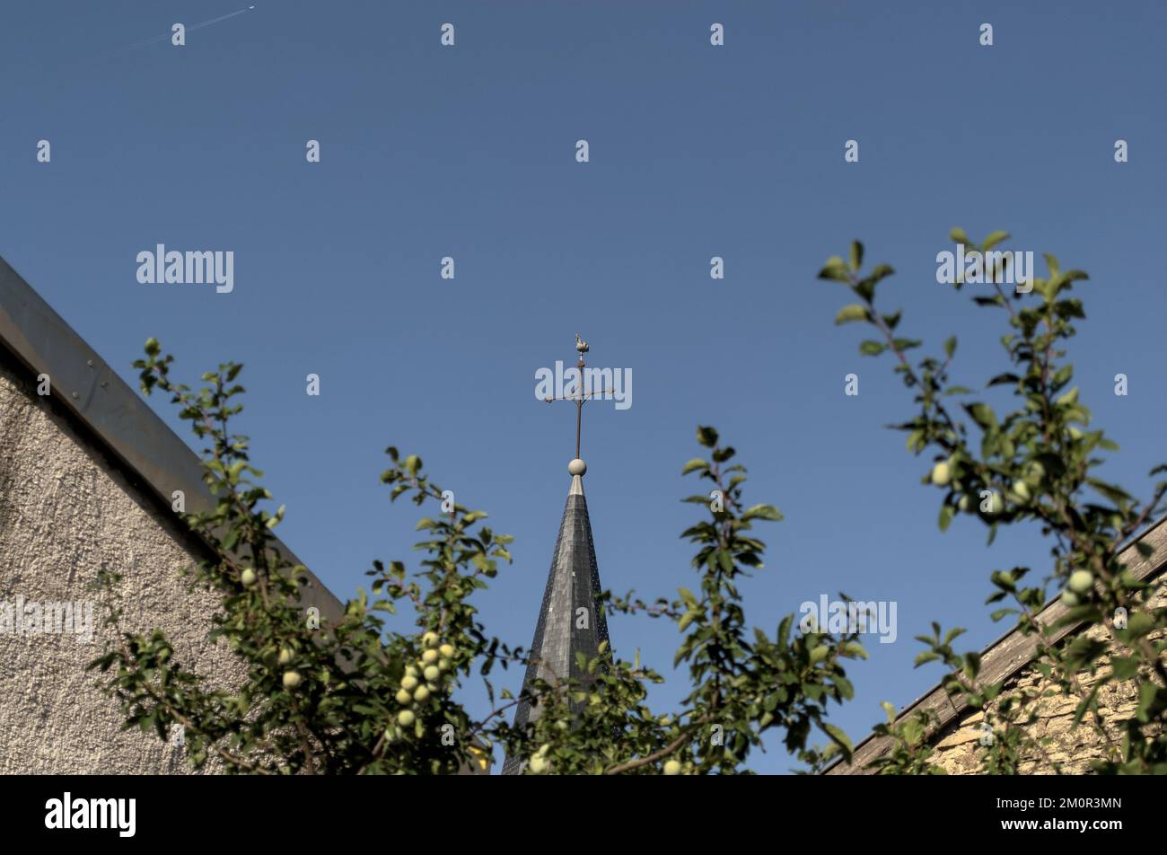 A tall-roofed church with a cross and rooster on it surrounded by ...
