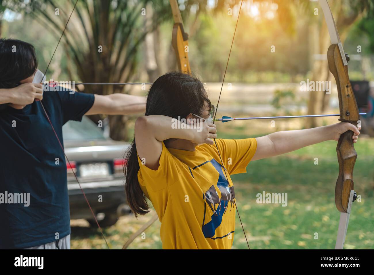 Back view of Asian girl wear eyeglasses with face mask aims archery bow ...