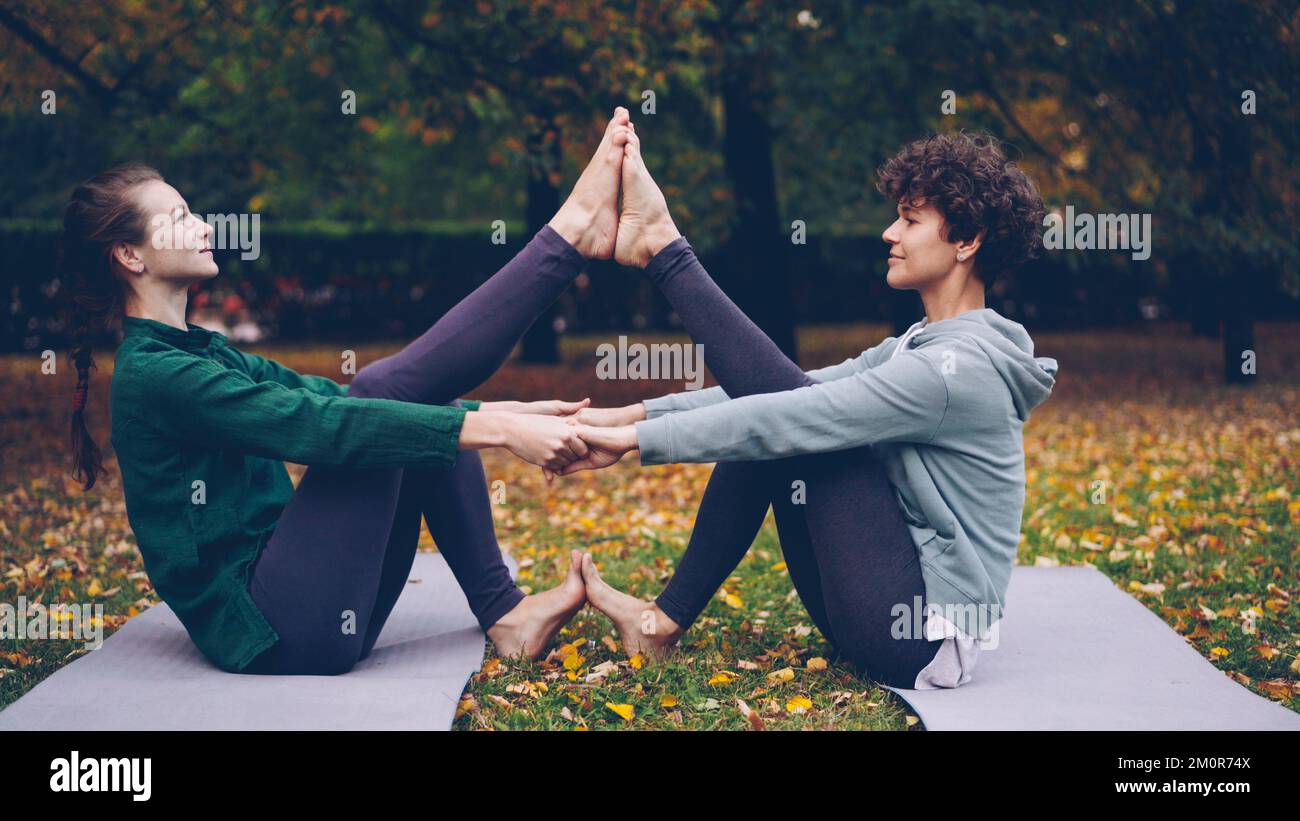Attractive girls are doing yoga exercises in pair holding hands and ...