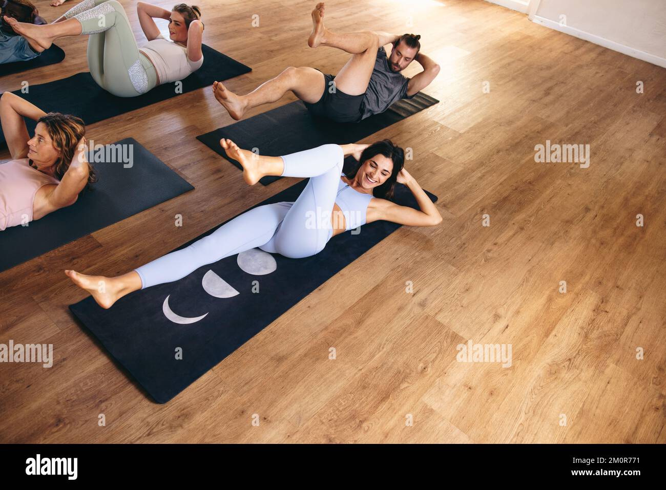 Happy young woman smiling while doing bicycle crunches with her class ...