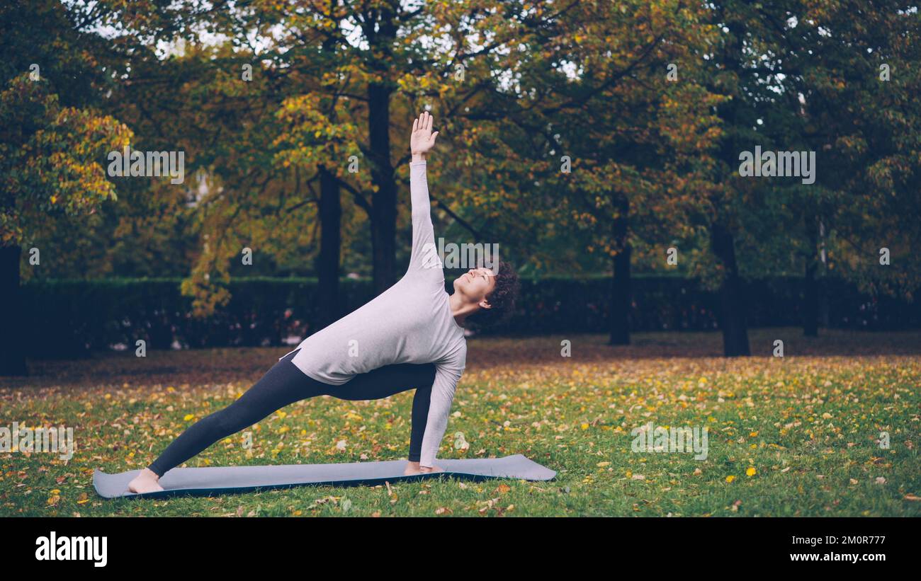 Beautiful girl with short curly hair is doing yoga outdoors stretching ...