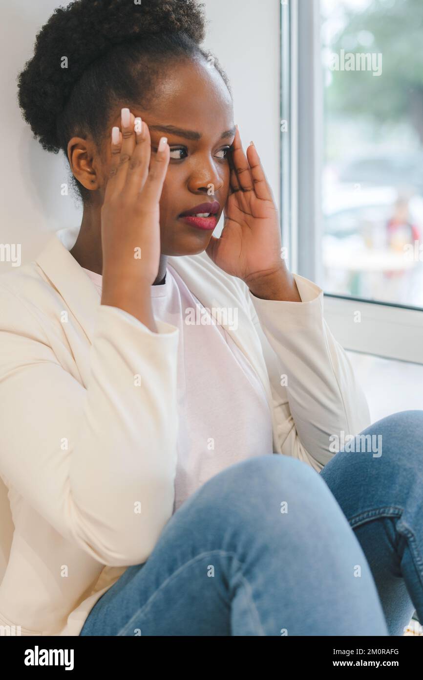 Worried african-american woman sitting near window at home alone. Sad ...