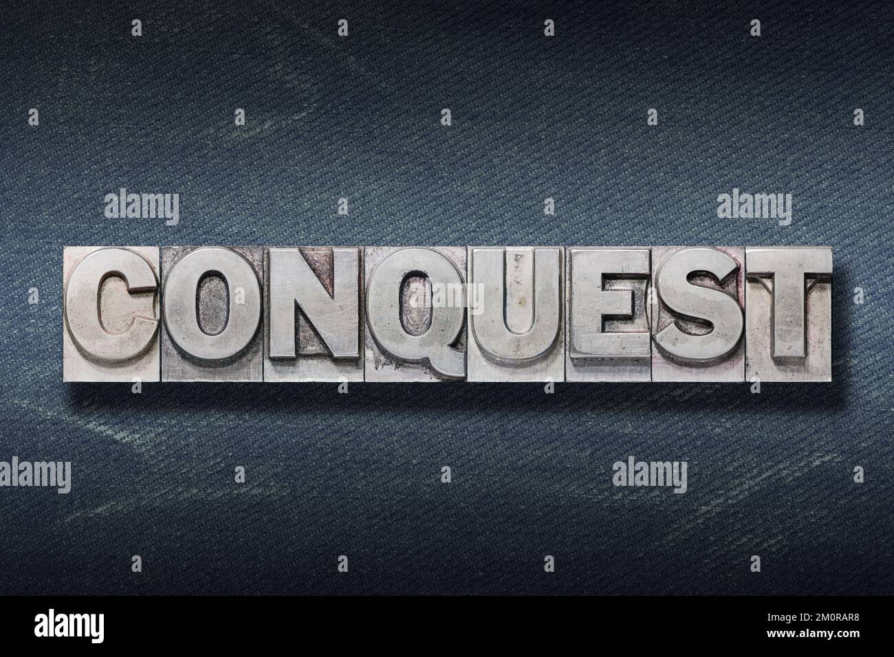 conquest word made from metallic letterpress on dark jeans background ...