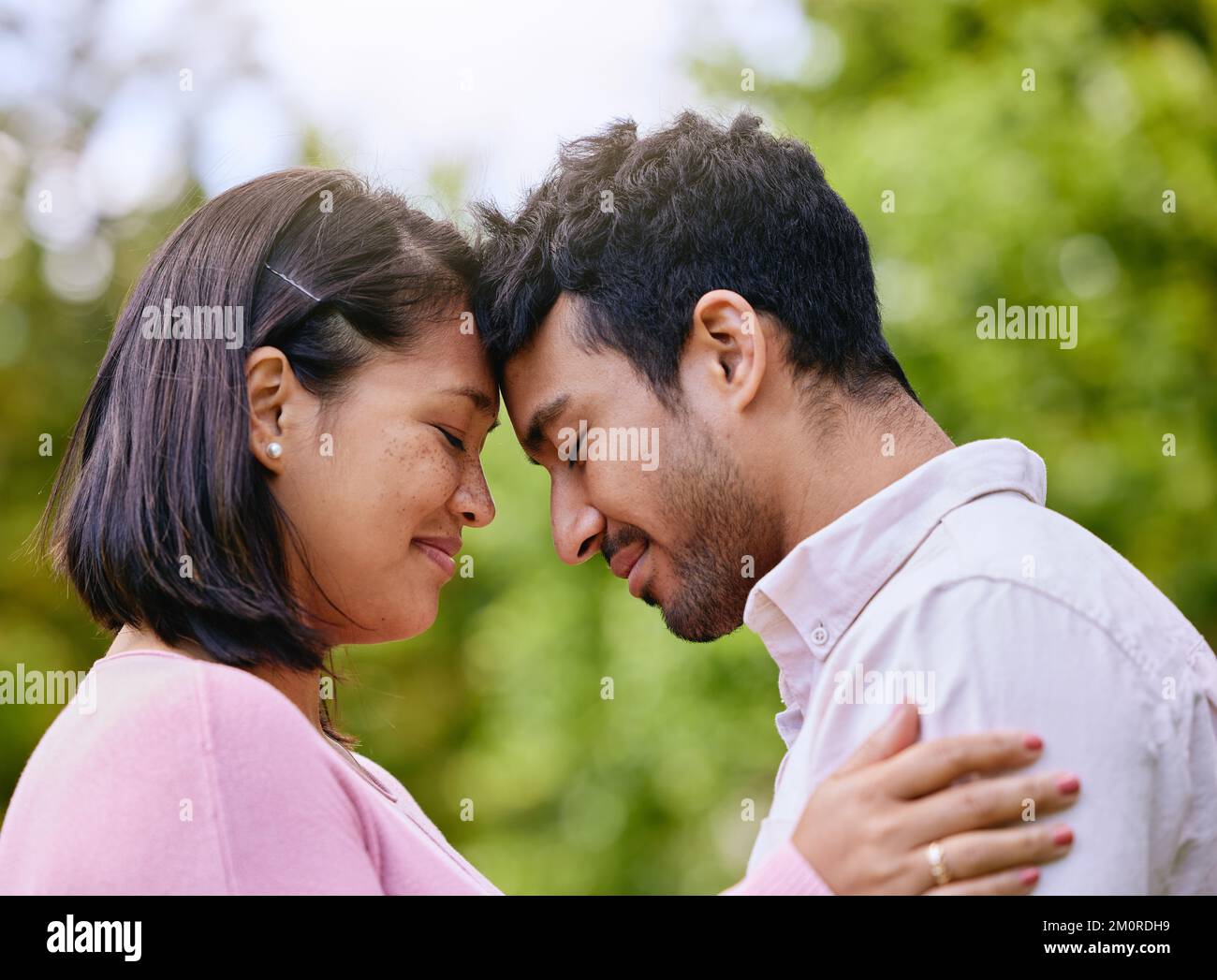Smiling Asian couple standing together with their foreheads touching ...