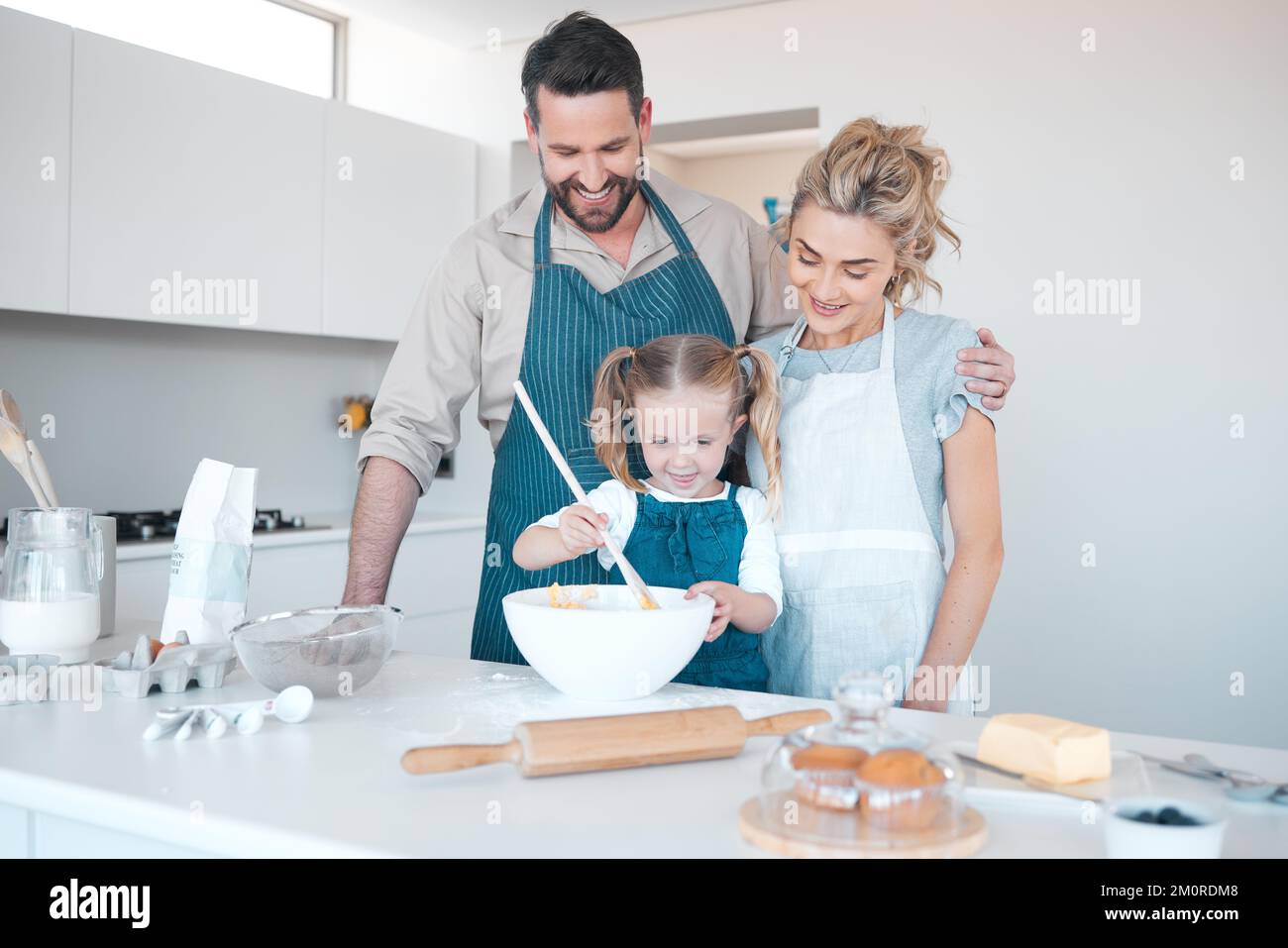 Happy parents watching their daughter bake. Little girl mixing a bowl ...