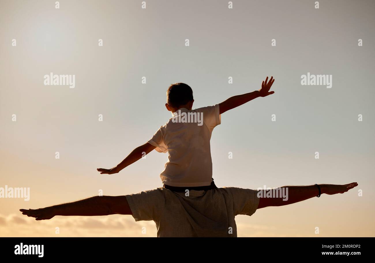 Silhouette of father carrying son on his shoulders at sunset. Rear view ...
