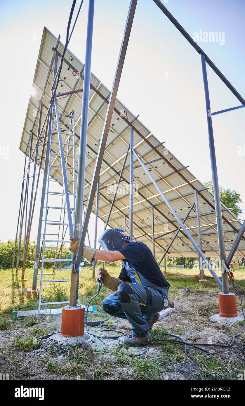Builder welding metal beam with welding machine for installing solar ...