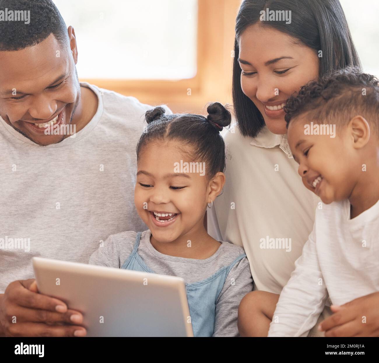 Happy mixed race smiling family of four bonding on a sofa while ...