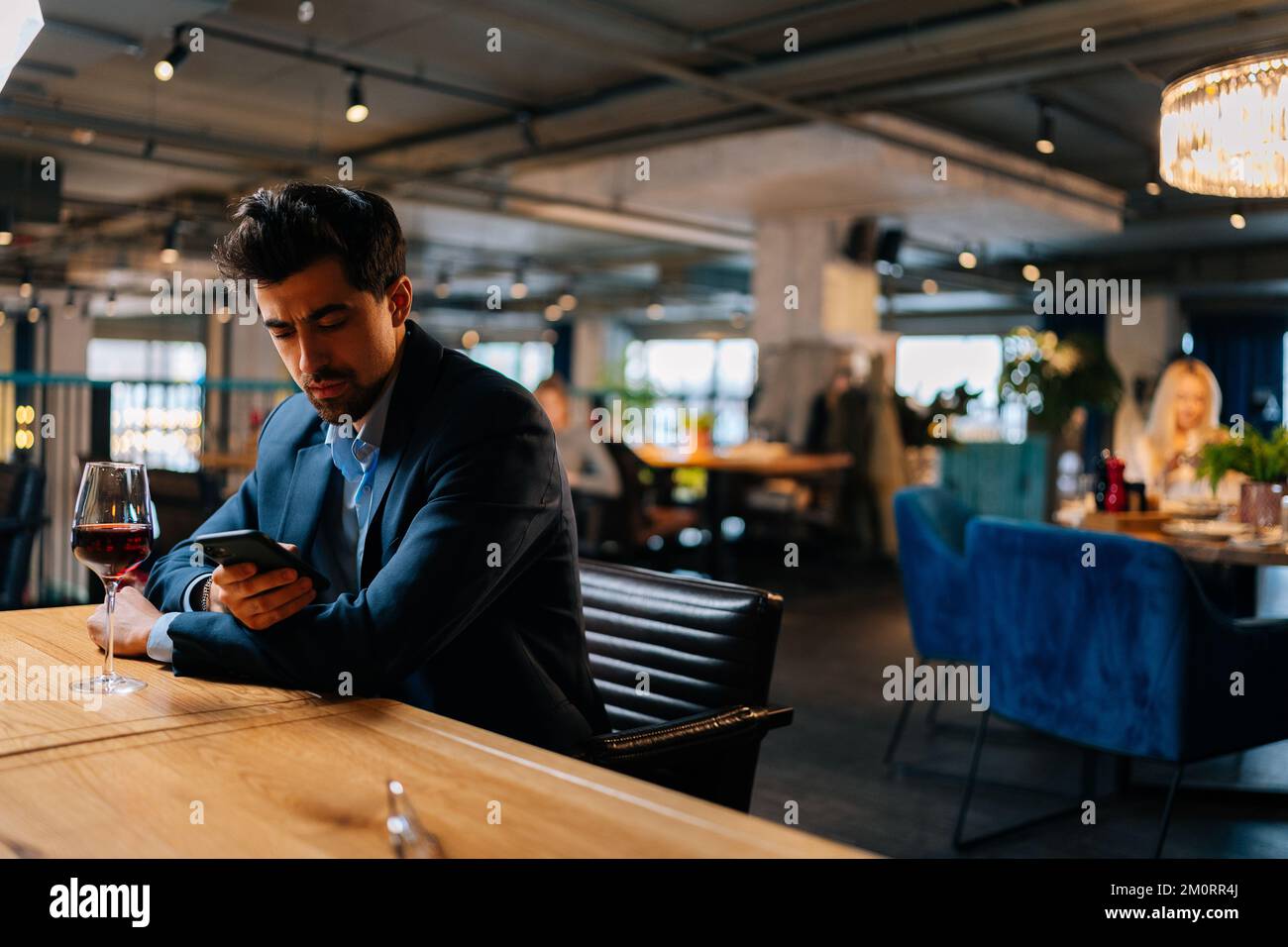Pensive elegant young man in suit using smartphone chatting with ...