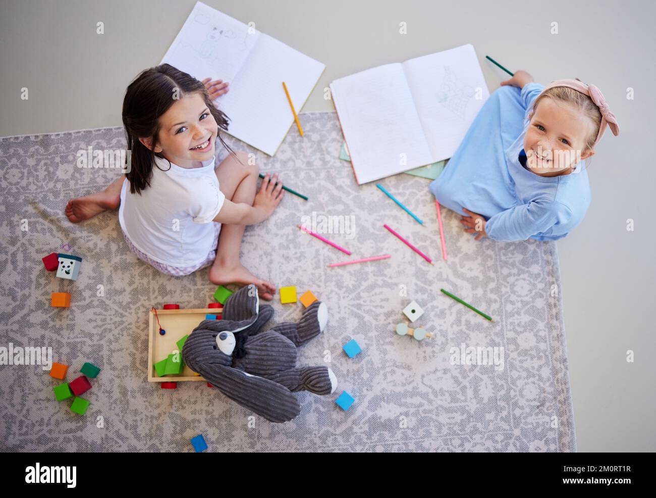 Adorable little girls drawing with colouring pencils at home from above ...