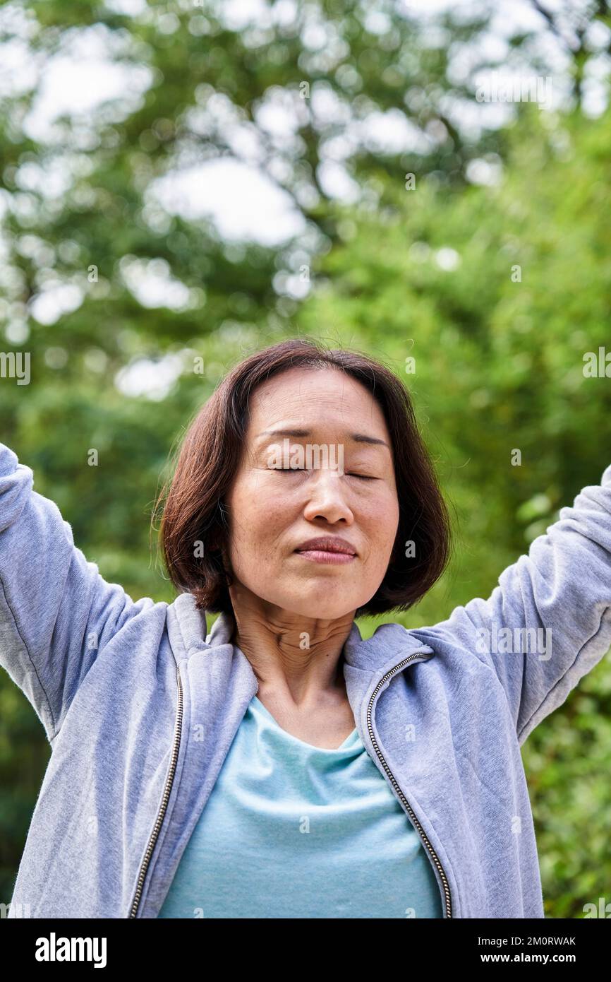 Senior Asian woman raising hands while taking a deep breath Stock Photo ...