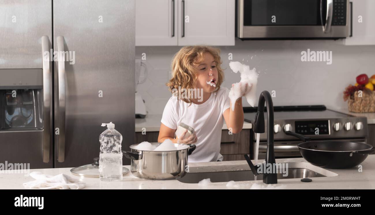 Home chores. Kid in kitchen cleaning plates. Cute boy washing dishes in ...