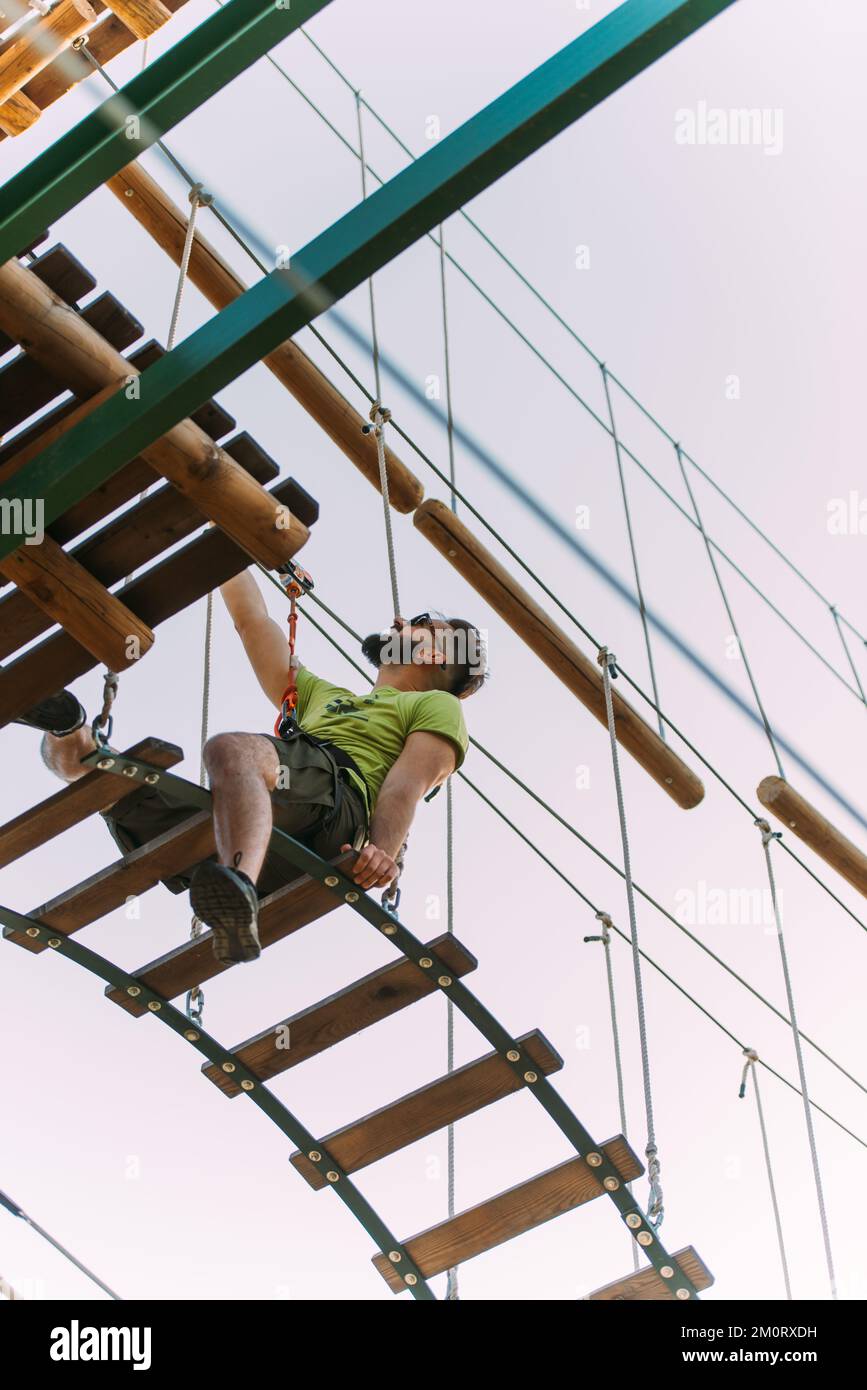 Handsome man balancing himself on the ladder in the adventure park ...