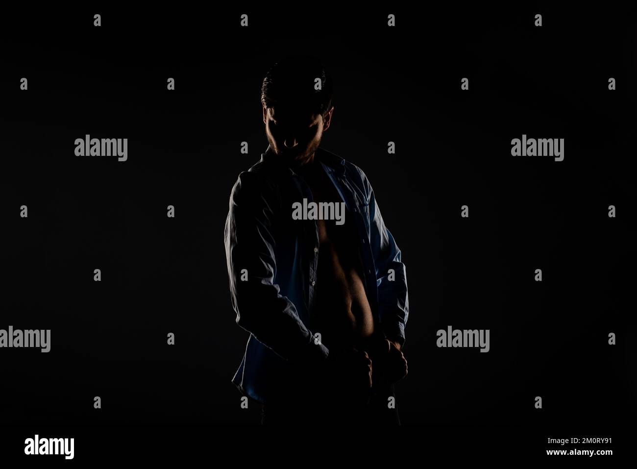 Handsome man in studio doing poses in a light dimmed room in front of ...