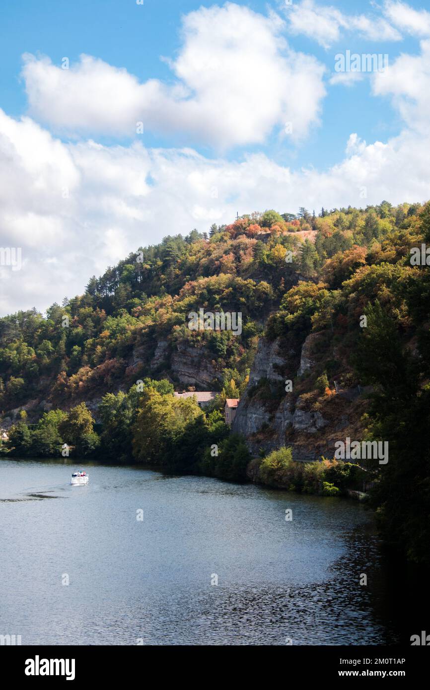 A vertical shot of a riverside covered in forests with a cloudy blue ...