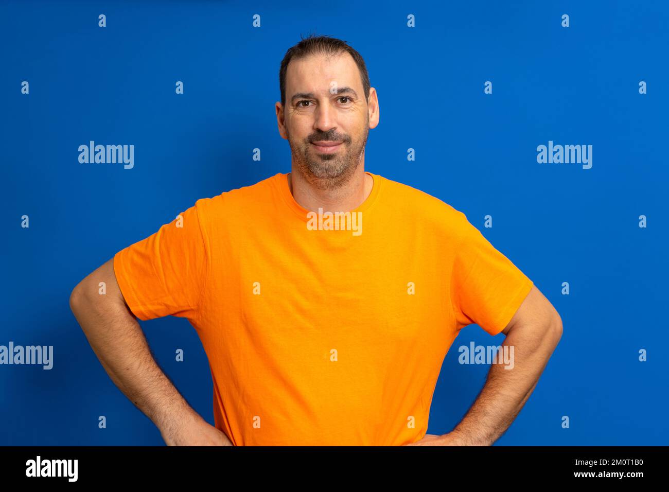 Cheerful bearded man in orange t-shirt posing isolated on blue ...