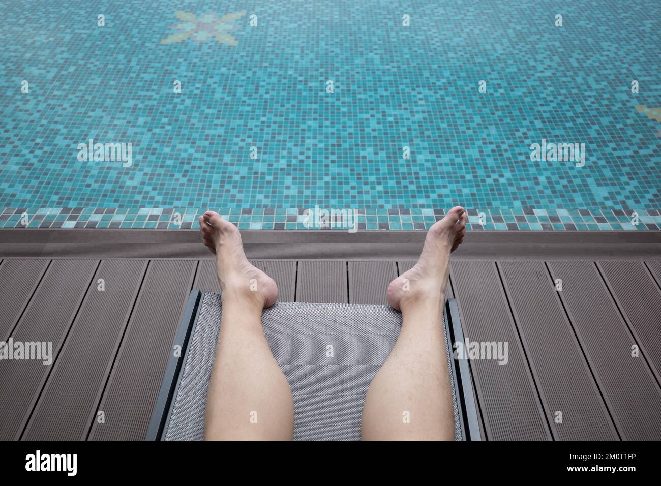 An adult male sitting on a deck chair by the side of a swimming pool on ...