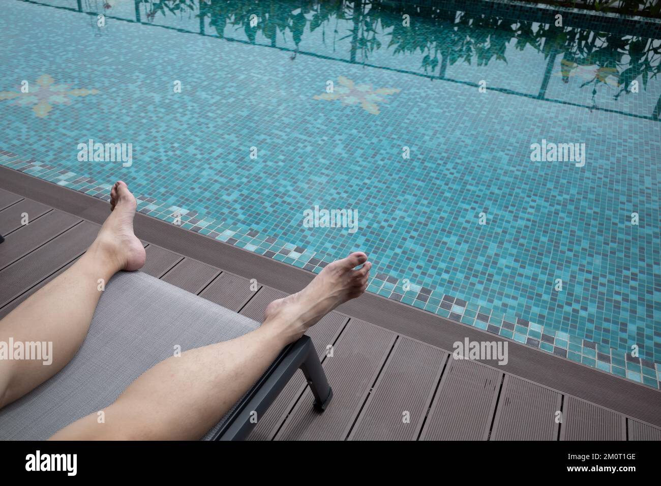 An adult male sitting on a deck chair by the side of a swimming pool on ...