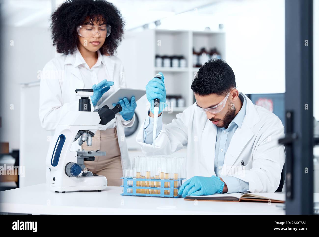 Two mixed race scientists wearing safety equipment while conducting ...