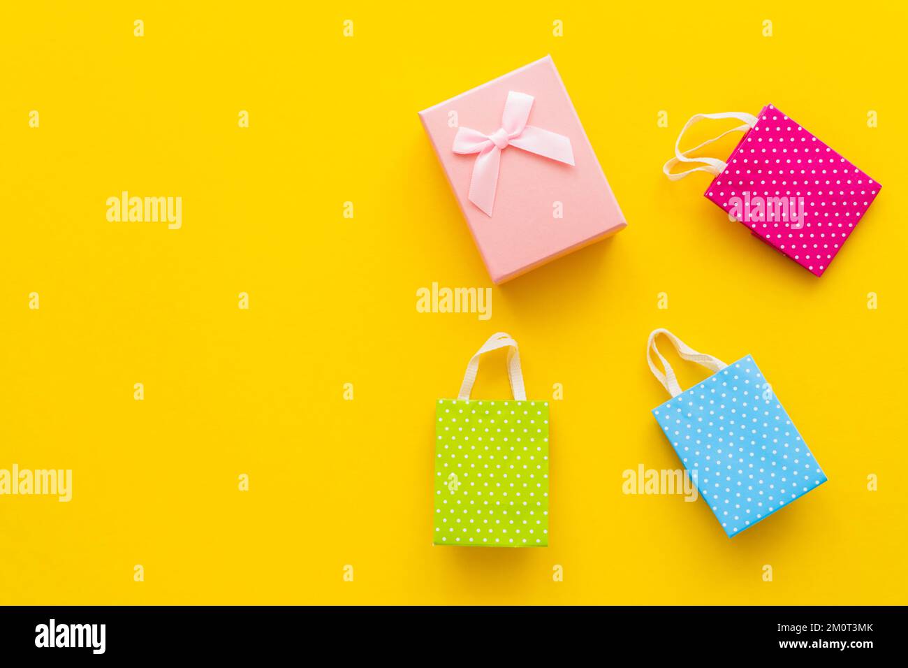 Top view of pink gift box and small shopping bags on yellow background ...