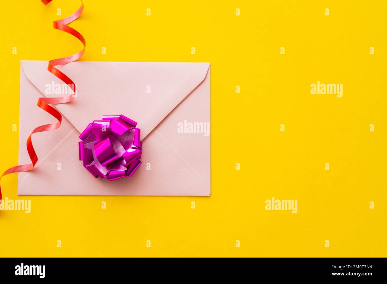 Top view of envelope and gift bow near serpentine on yellow background ...