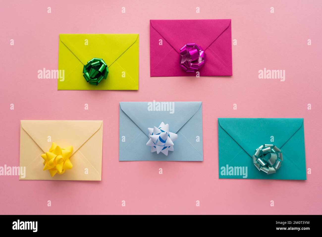Top view of colorful gift bows on envelopes on pink background,stock ...