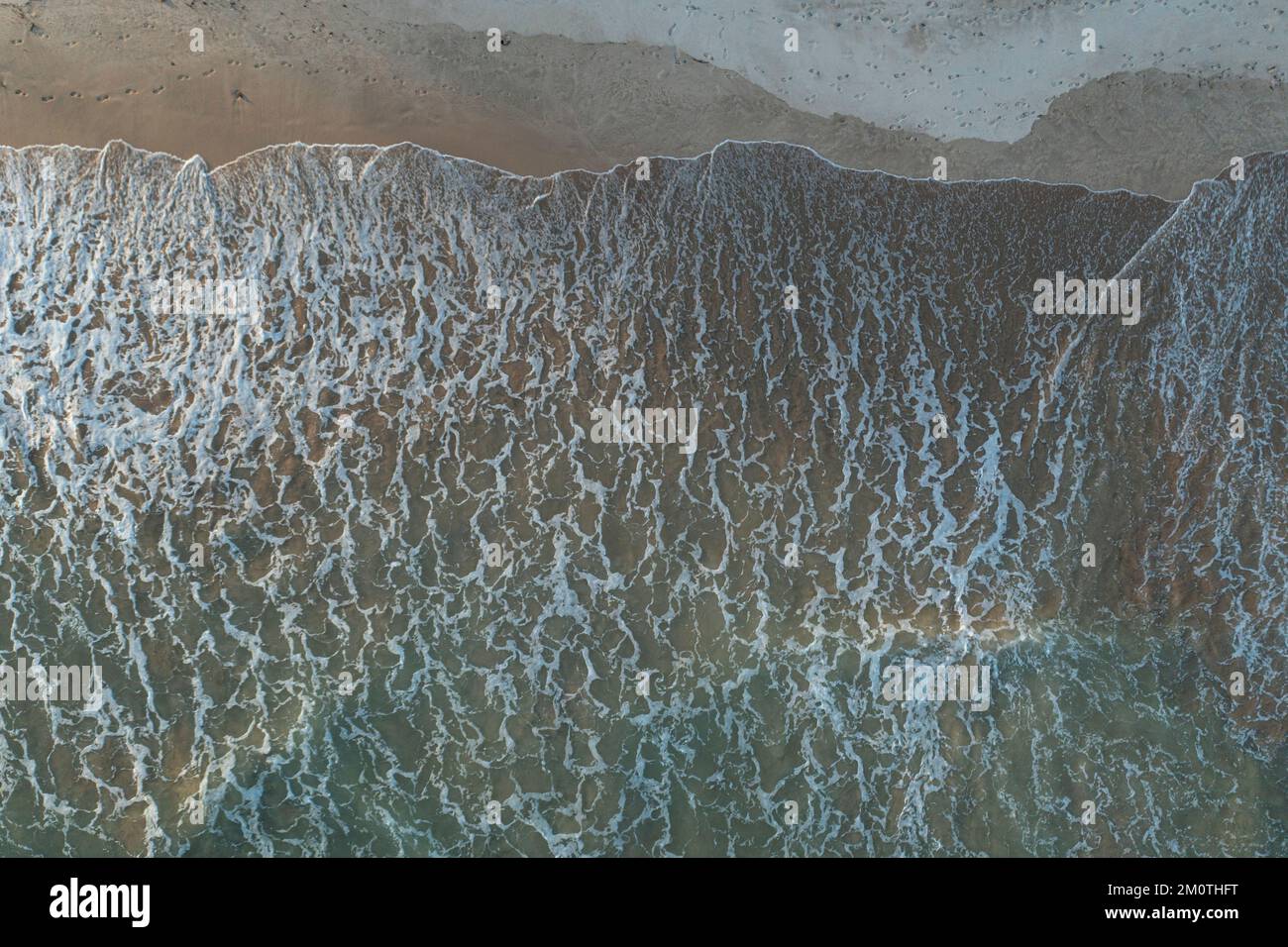transparent water wave reaching the beach sand and making foam - drone ...