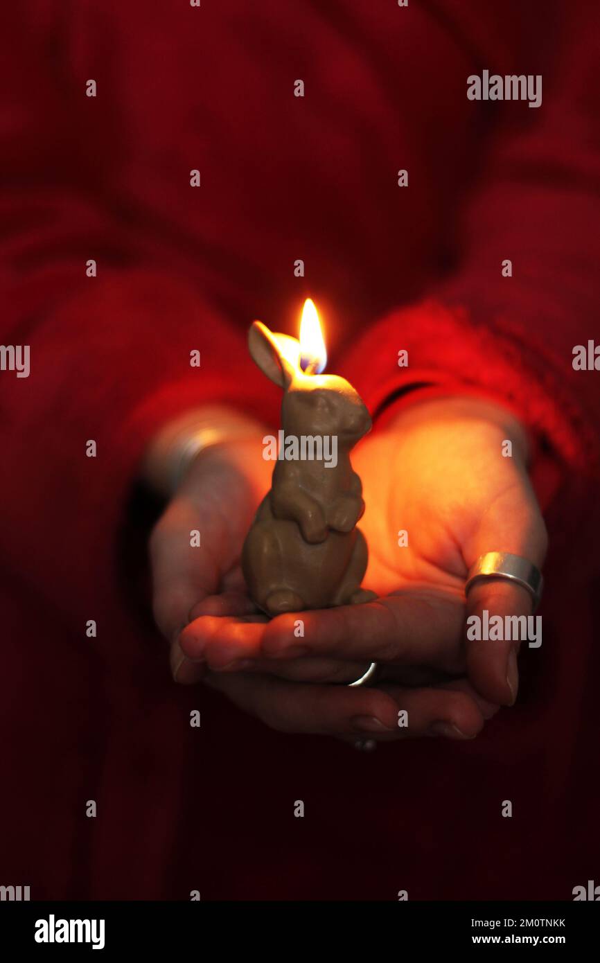 A burning candle in the shape of a hare in his hands. Holiday advent ...