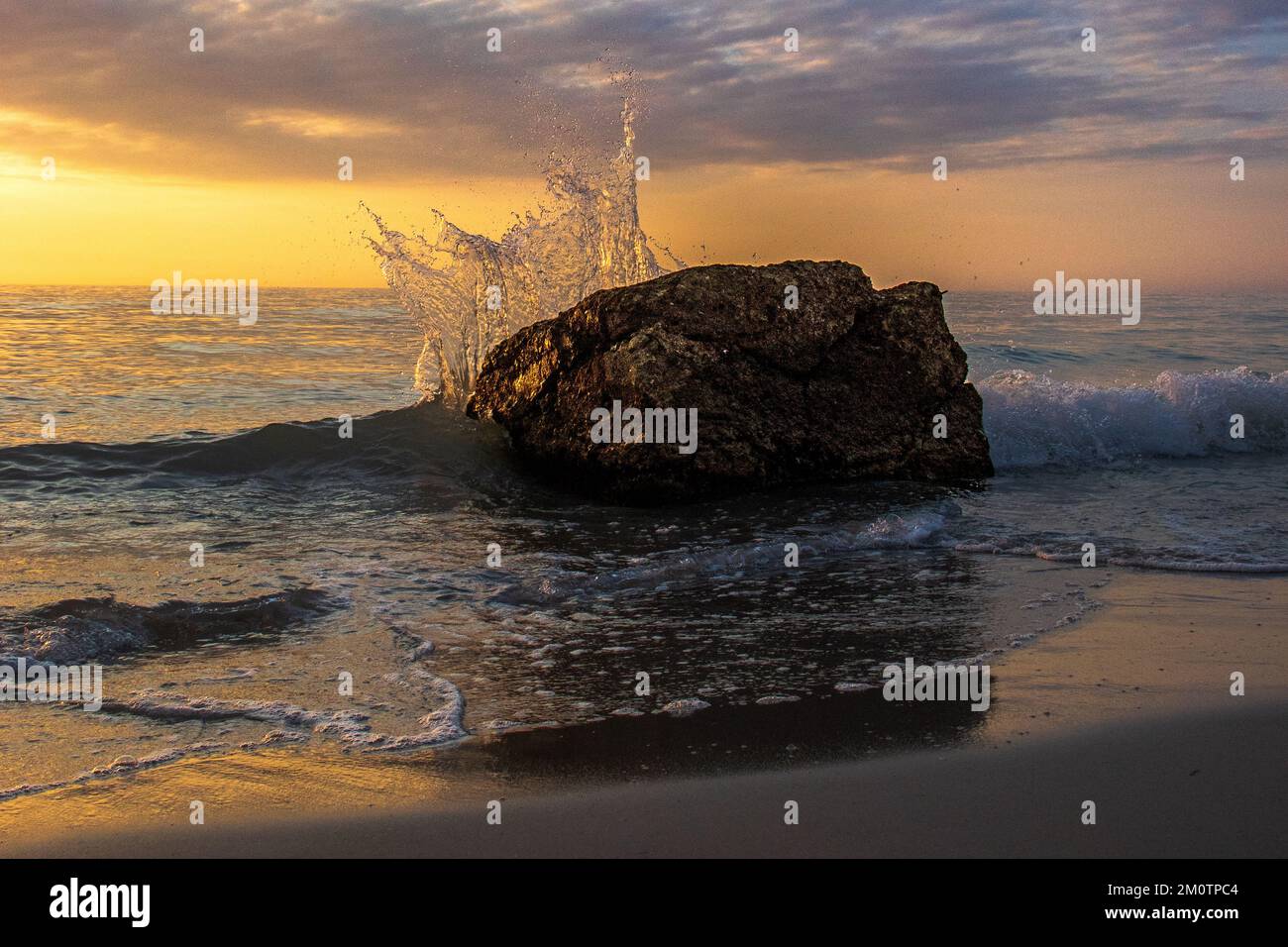 Wave hits stone in the Ocean in the sunsetlights Stock Photo - Alamy