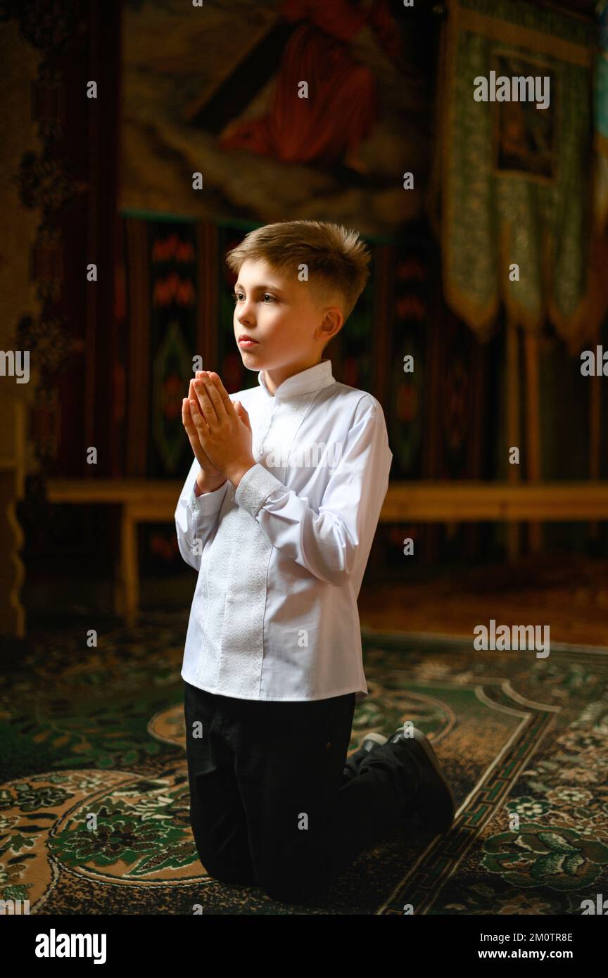 A boy is kneeling in prayer to God, children's prayer in the church ...