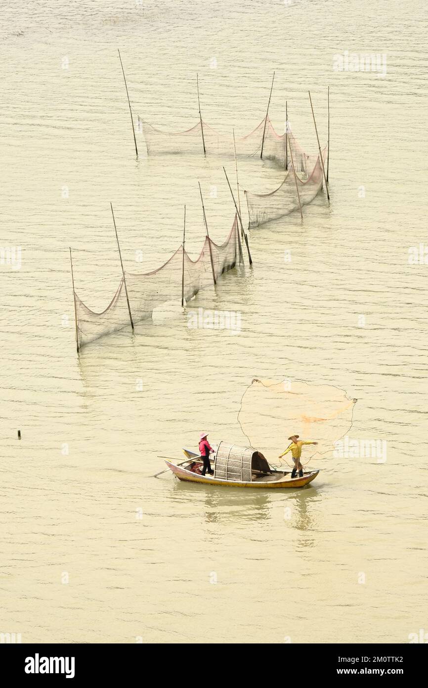 A vertical shot of two men on a boat throwing net to catch fish Stock ...