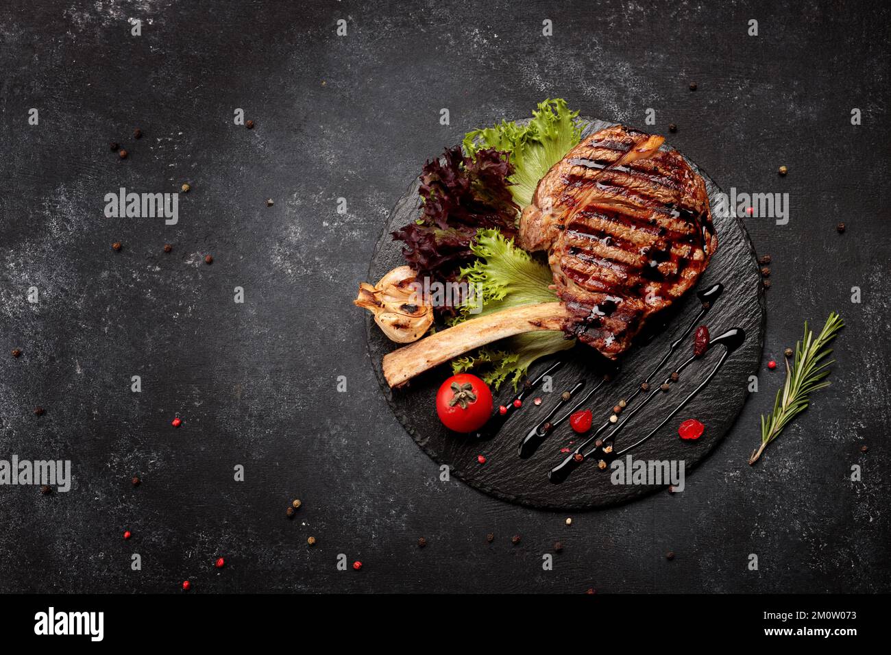 Tomahawk steak on the bone, with herbs, tomatoes and garlic, on black ...
