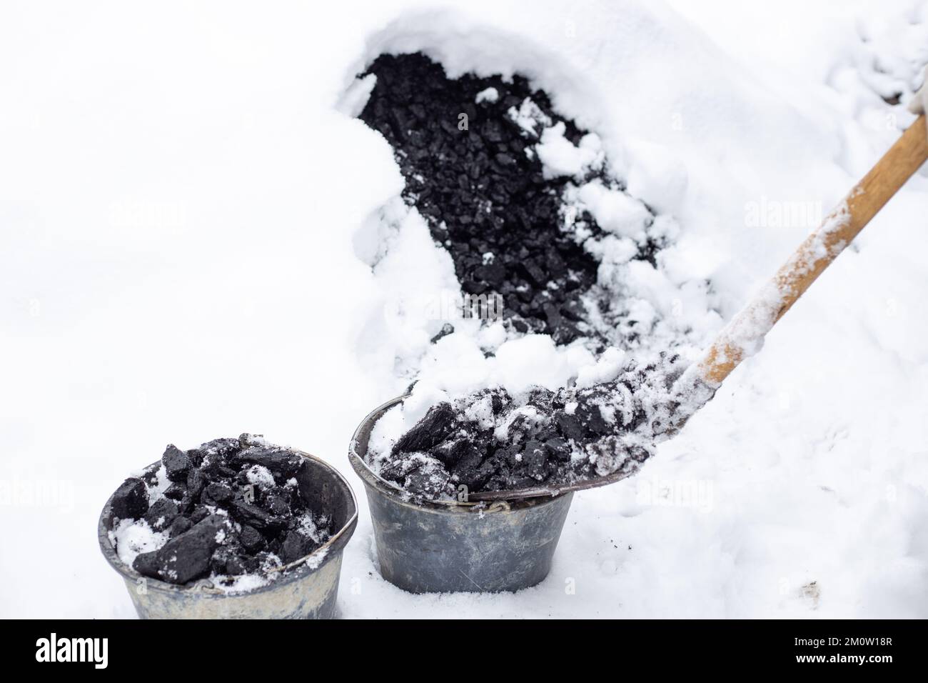 A man puts coal into buckets with a shovel on a winter cold snowy day ...