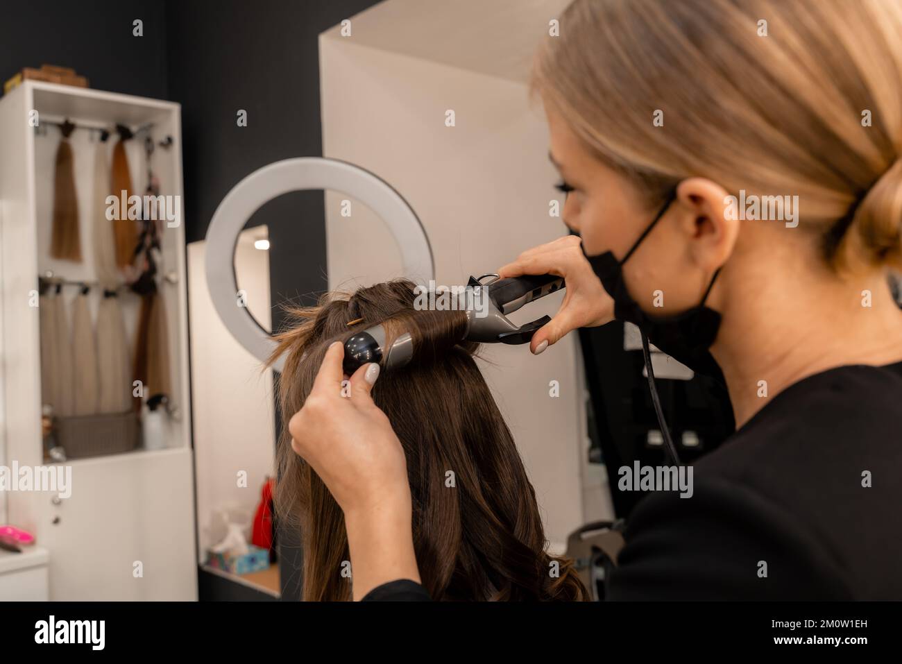 A hairdresser in a black mask prepares a woman, makes a hairstyle with ...