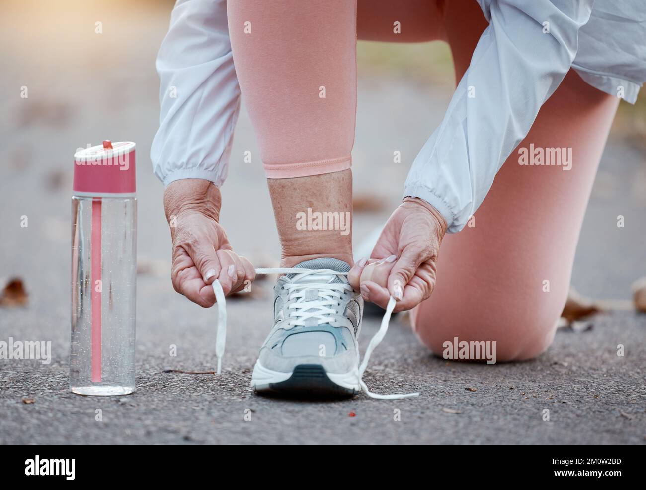 Senior woman fitness, exercise and shoes with hands tying laces while running on a concrete road ...