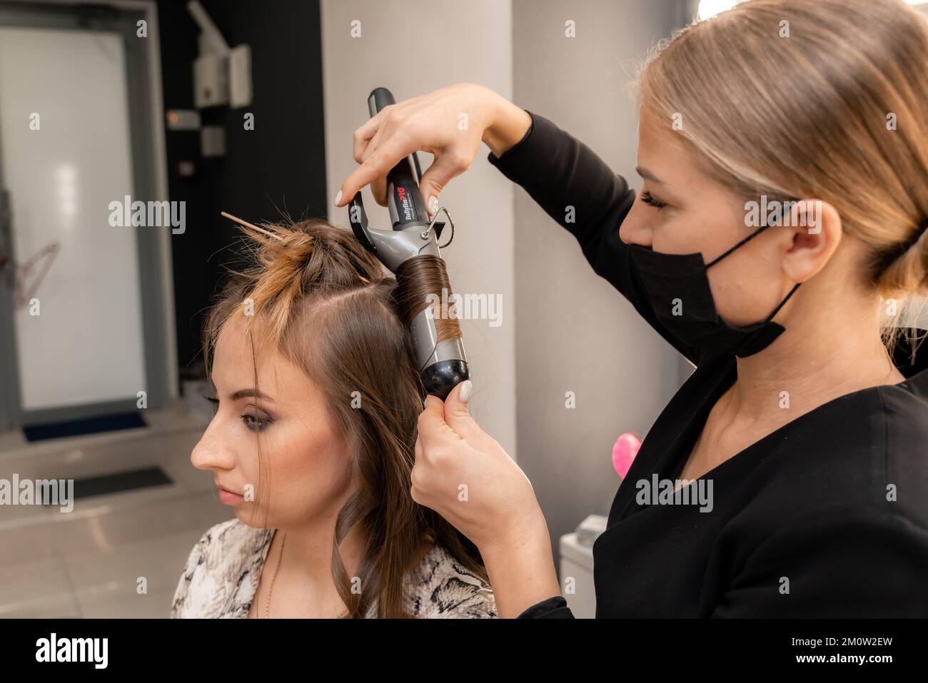 A hairdresser in a black mask prepares a woman, makes a hairstyle with ...