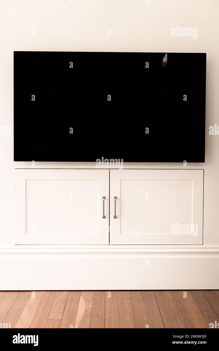 The vertical shot of a modern TV screen over a white cabinet doors on ...