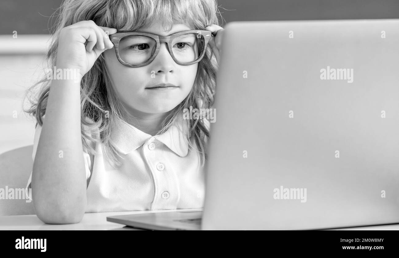 small kid boy in glasses study online in school classrrom with computer ...
