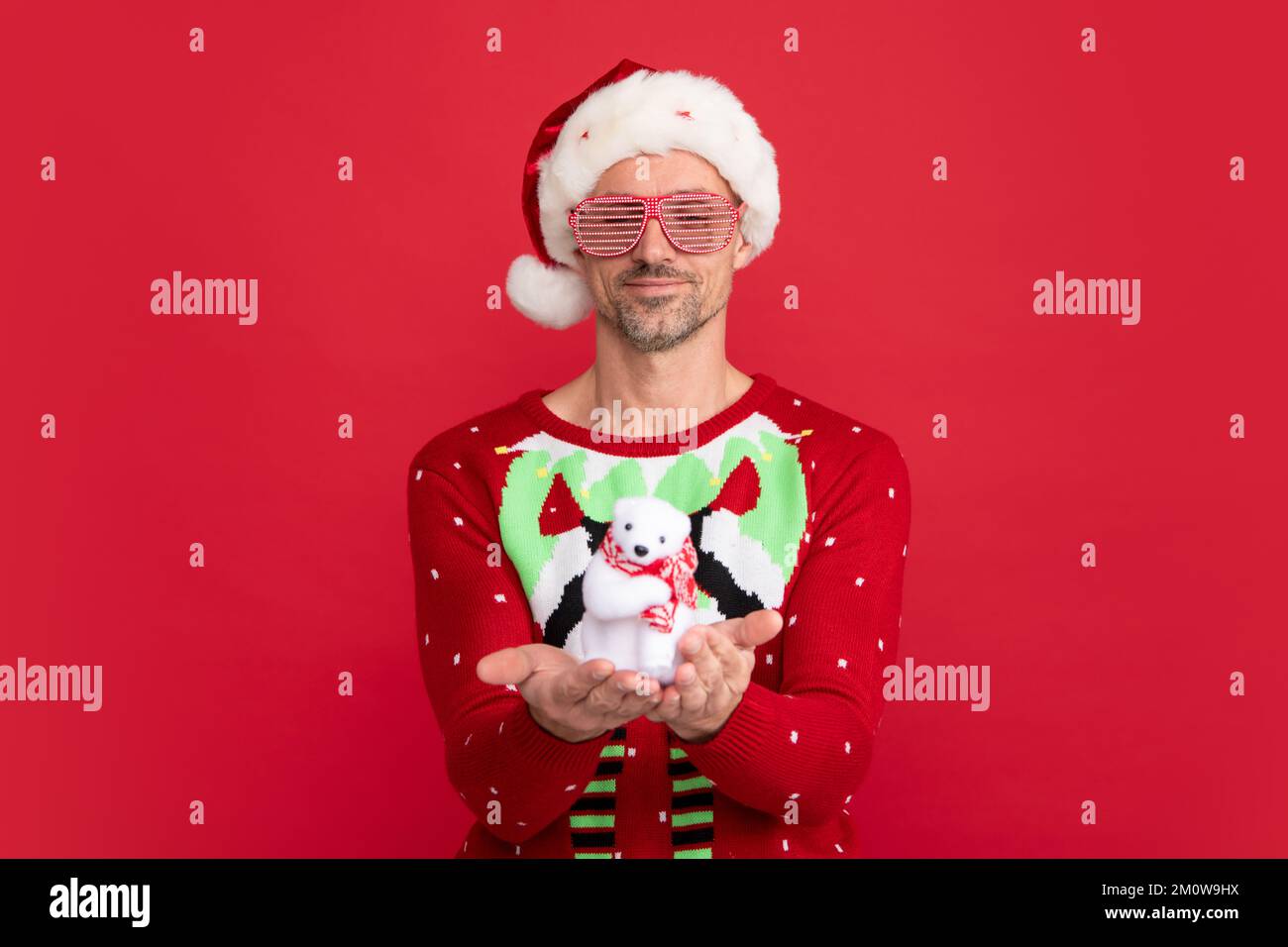 Santa hold christmas toy. Man in Christmas sweater and Santa hat on red ...