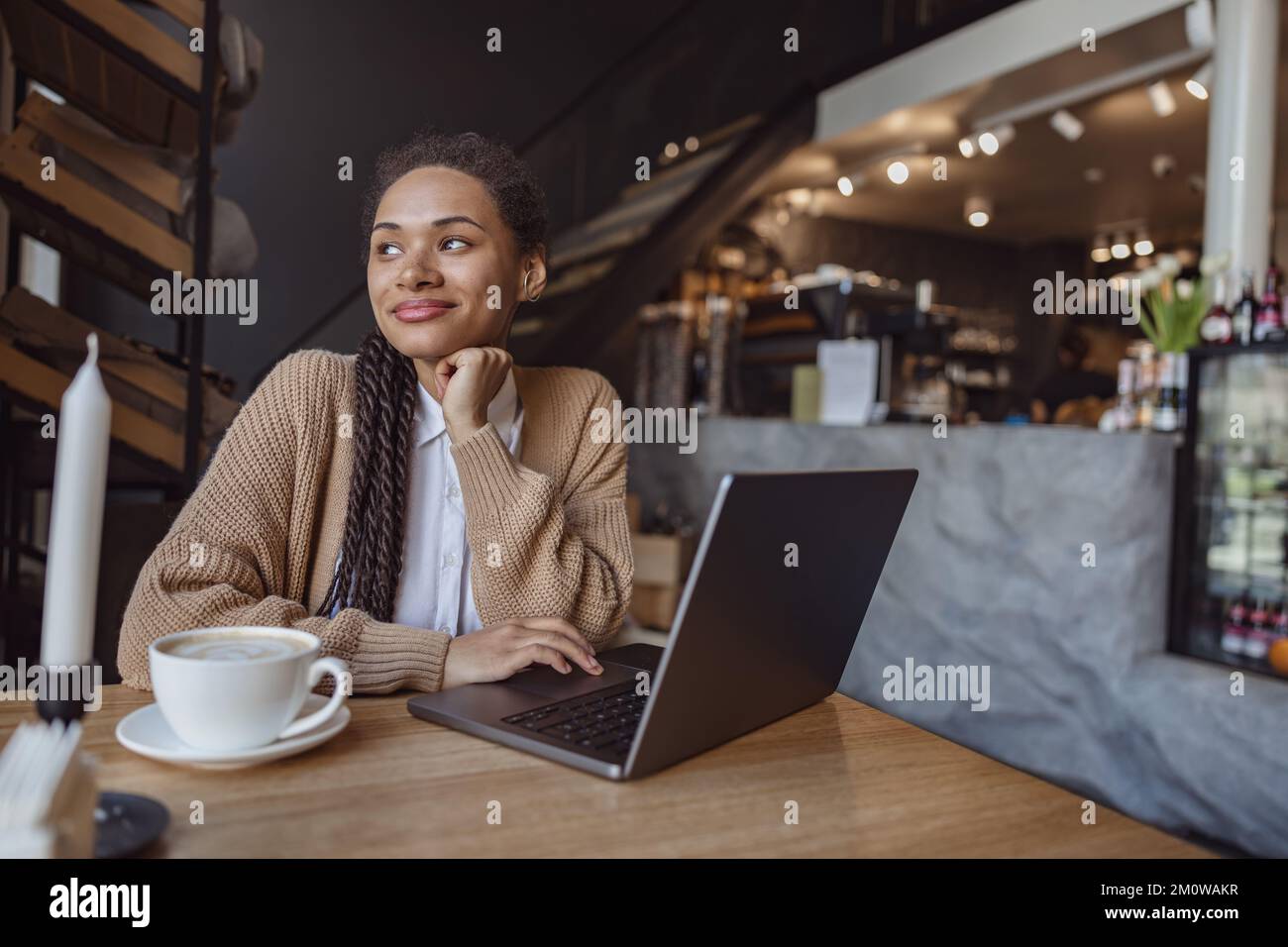 Charming pensive African American woman in casual wear enjoying remote ...