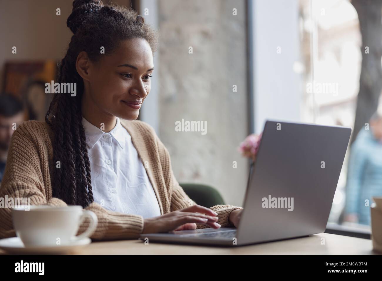 Adorable African woman student types text on laptop keyboard, works, studies, doing research or ...