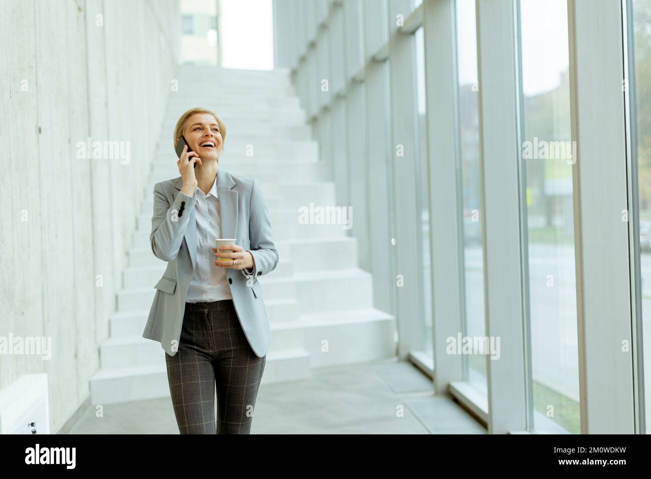 Businesswoman using mobile phone while walking on the modern office ...